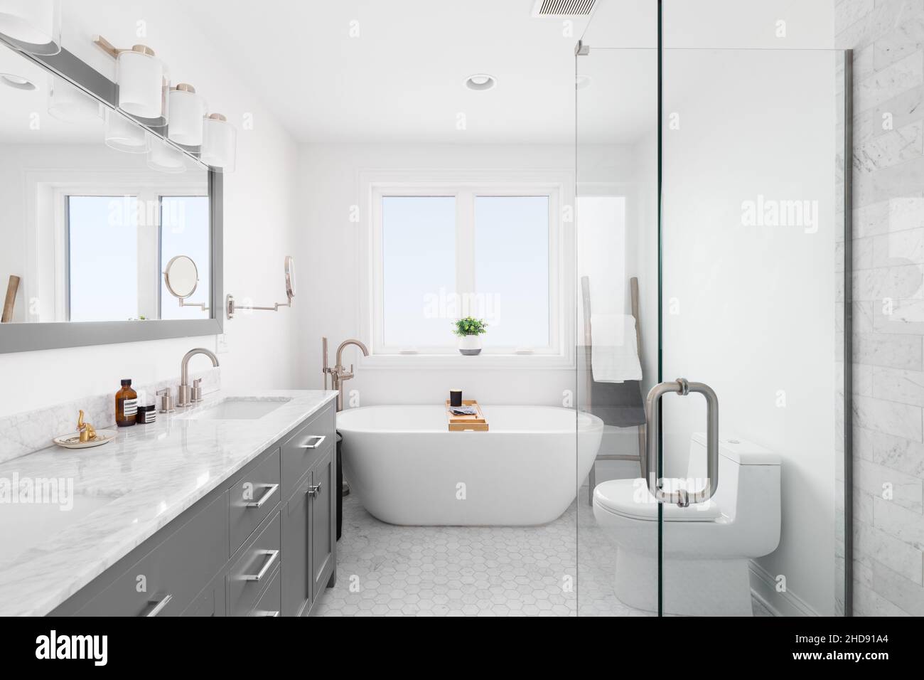 A beautiful bathroom with a grey vanity cabinet, hexagon marble tile flooring, standalone tub ...