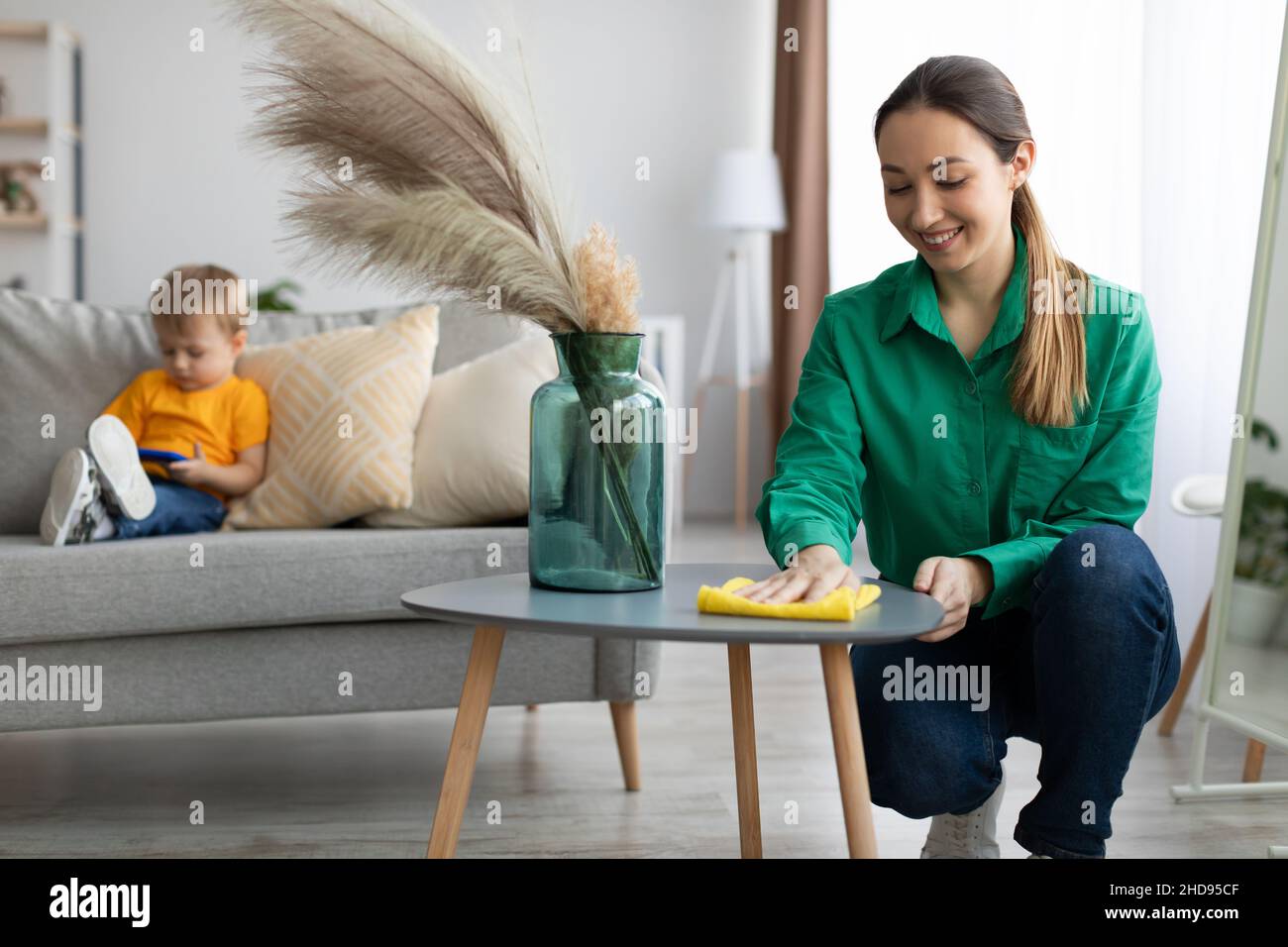 Young mother dusting off coffee table and tidying up at home while ...