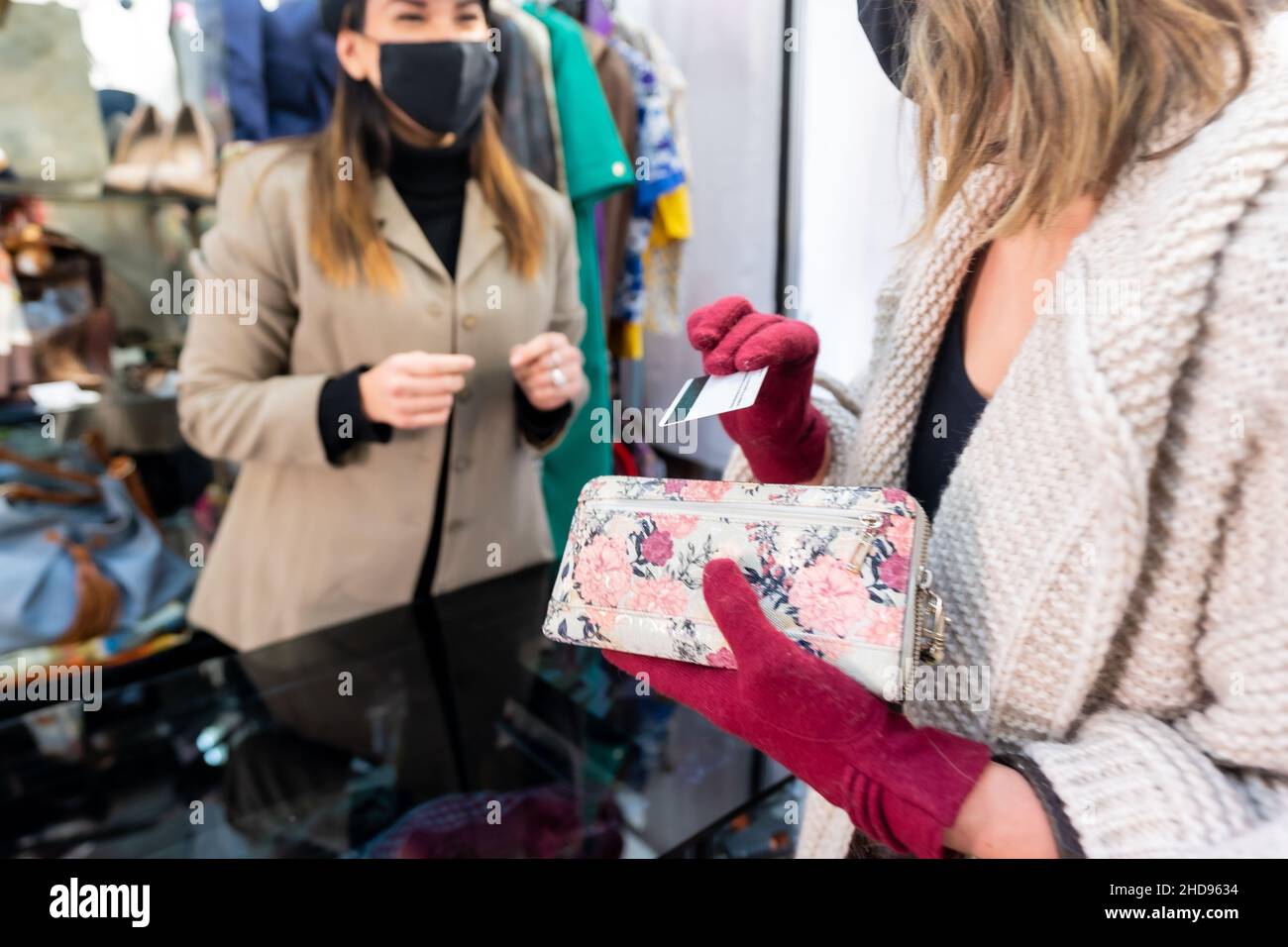 Client paying with a mask to an employee with masks in a clothing store ...
