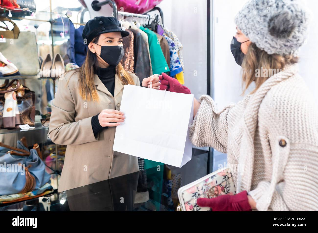 Employee with masks in a clothing store handing over clothes to a ...