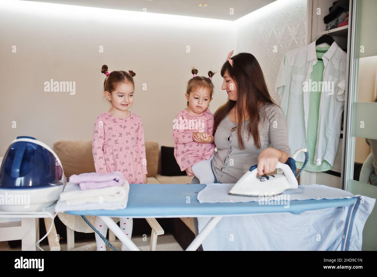 Woman mother and her two daughters child girls as little helper ironing ...