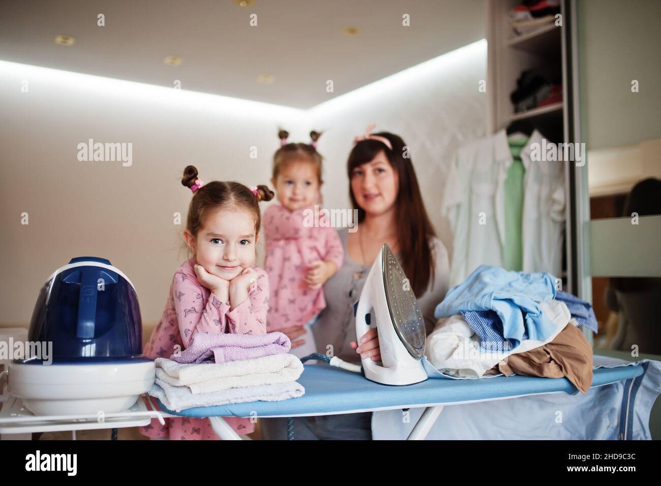 Woman mother and her two daughters child girls as little helper ironing ...