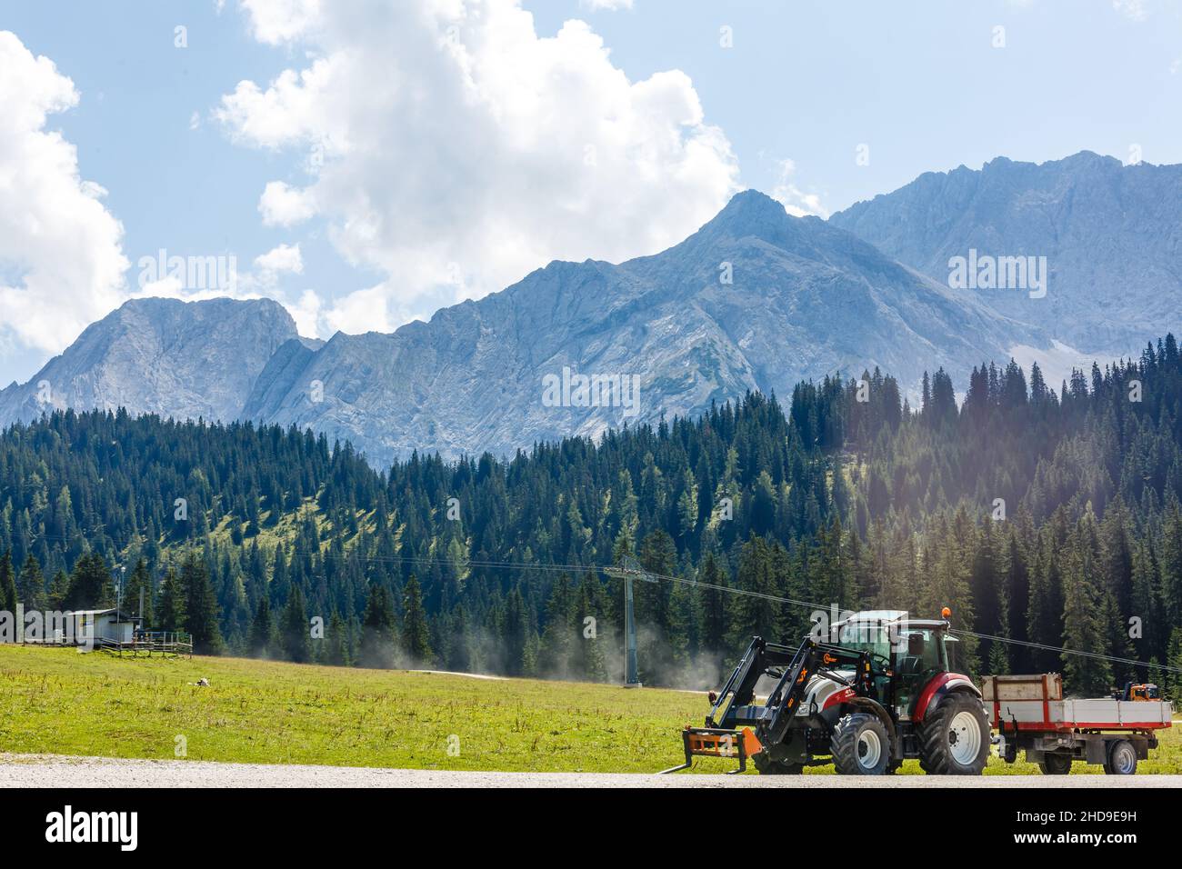 Harvesting crop by red tractor in austrian alpine green mountain fields ...