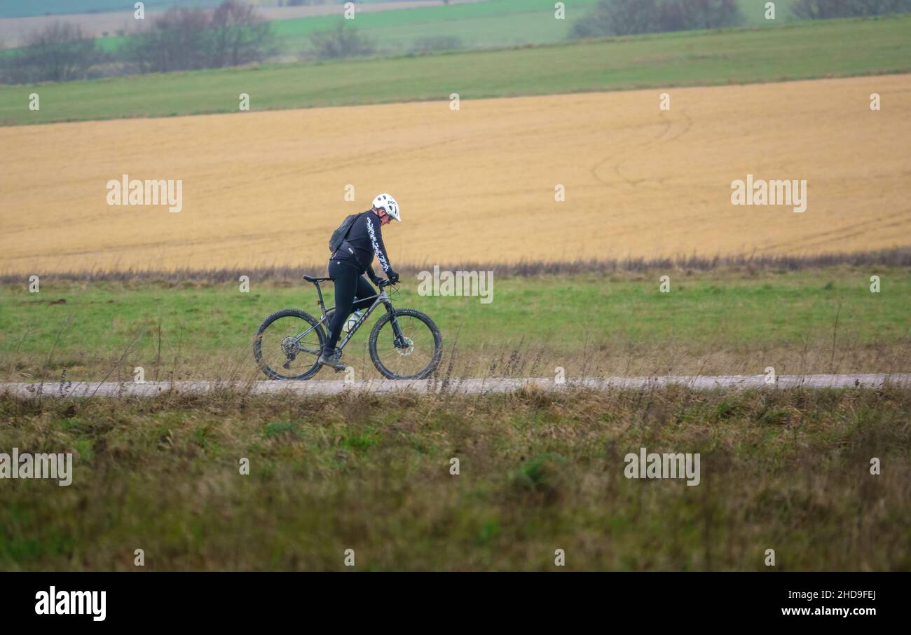 a casual peddle bike cyclist riding along an unmade track crossing open ...
