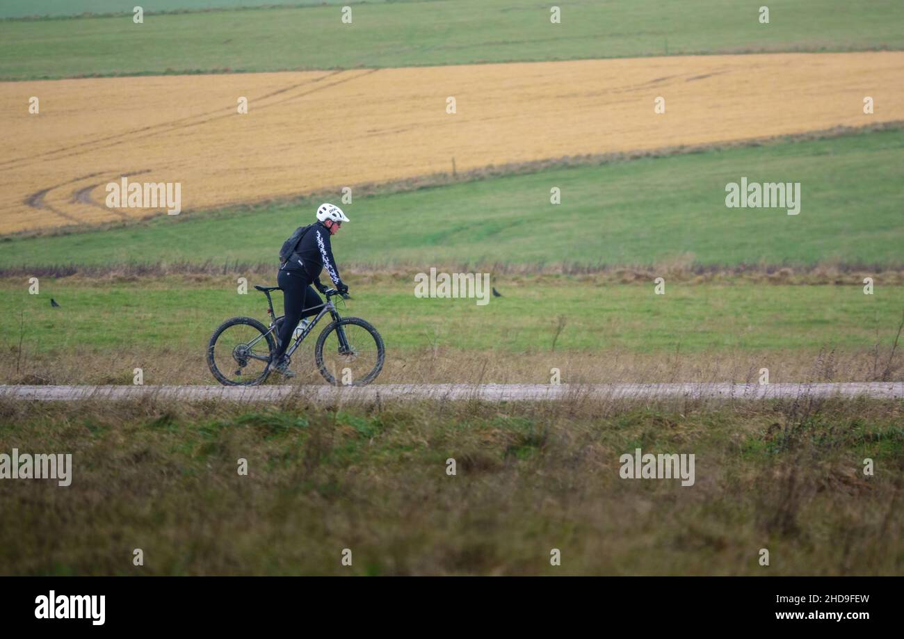 a casual peddle bike cyclist riding along an unmade track crossing open ...