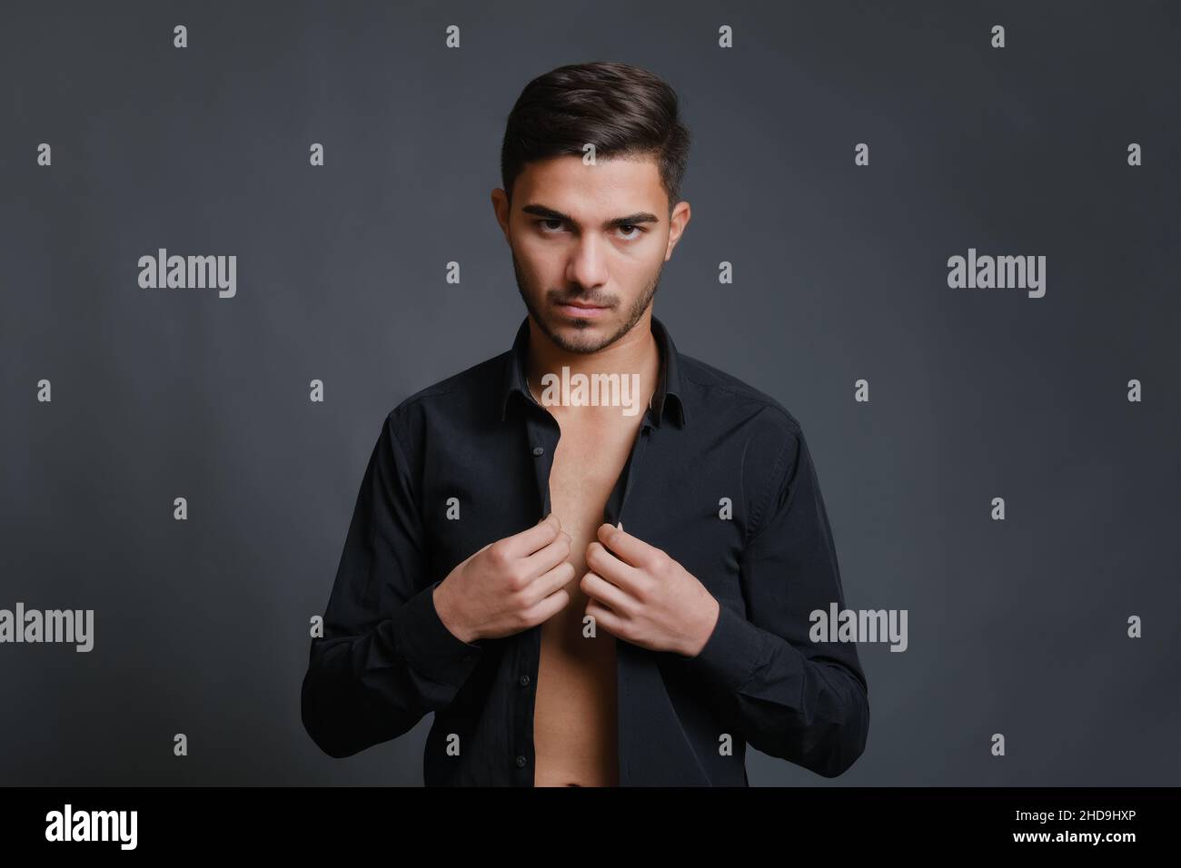 Portrait of unshaven young man buttoning up black shirt Stock Photo - Alamy