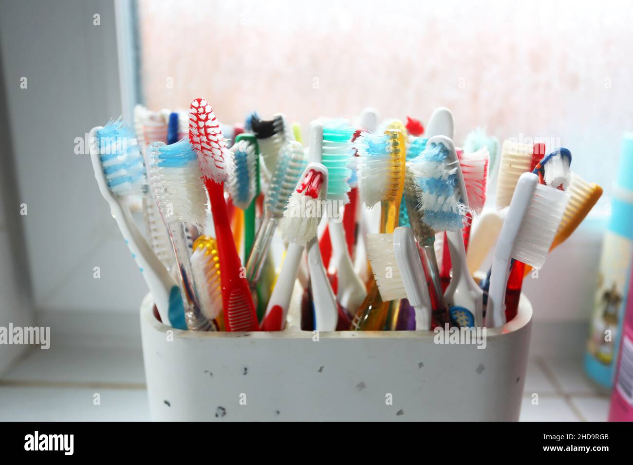 A selection of colourful plastic toothbrushes in a pot in a bathroom in ...