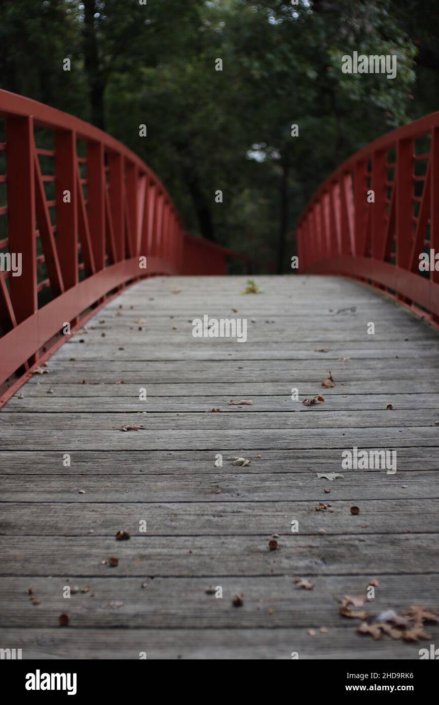 Fall leaves on a bridge with a wooden floor and red metallic railings ...