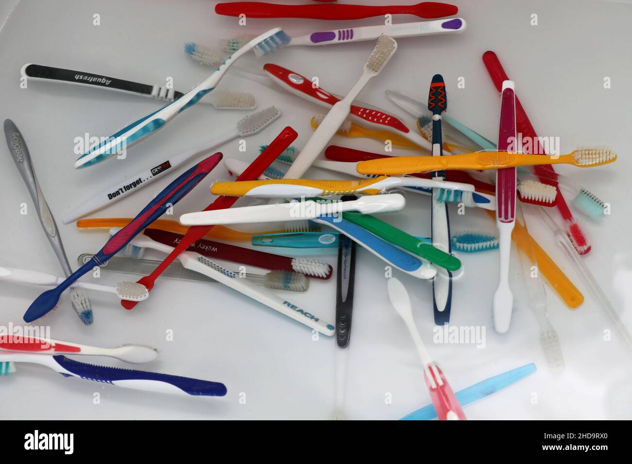 A selection of colourful plastic toothbrushes in a pot in a bathroom in ...