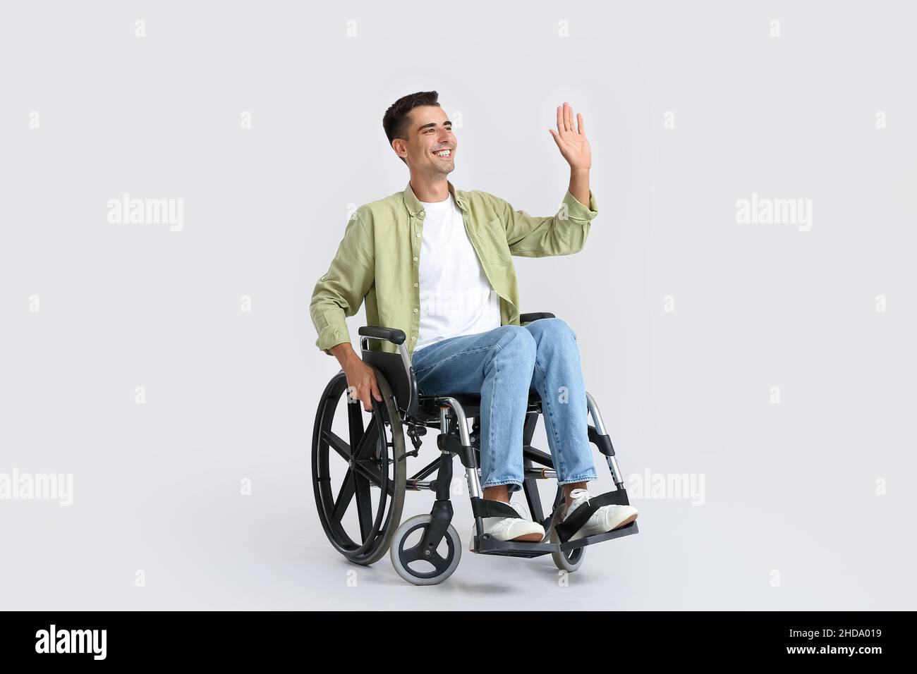 Young man in wheelchair waving hand on light background Stock Photo - Alamy