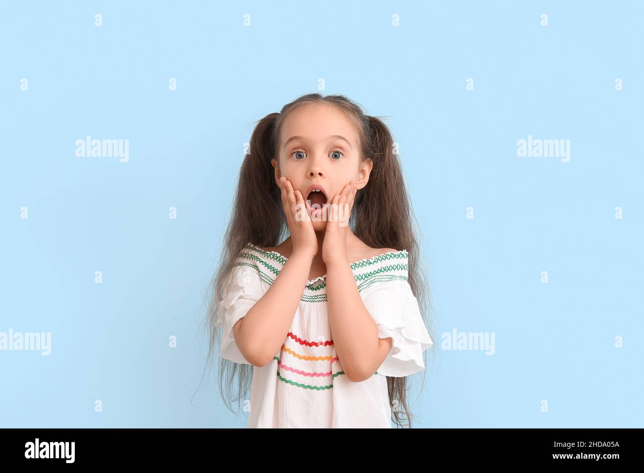 Portrait of shocked little girl with ponytails on blue background Stock ...