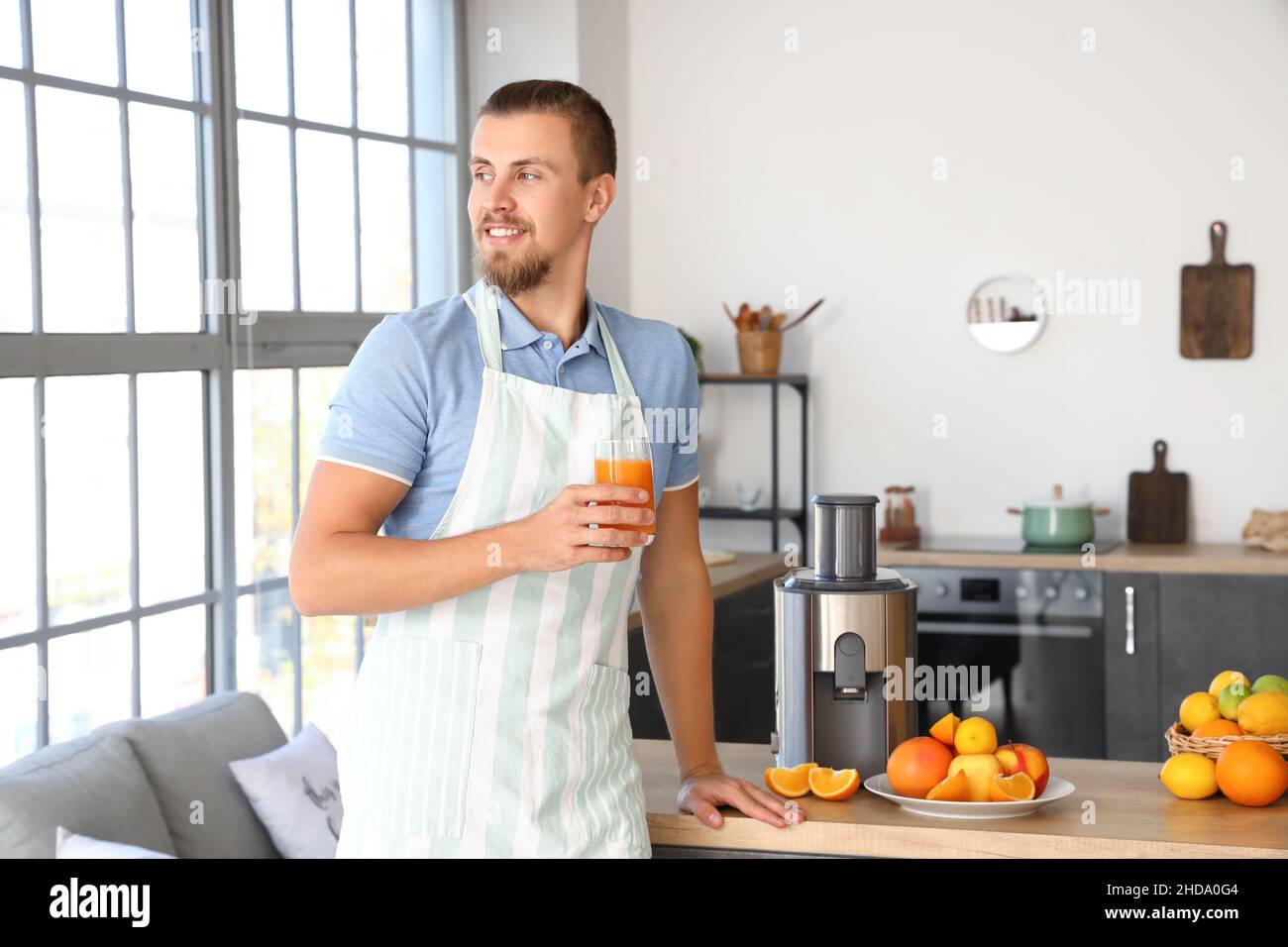 Young man with glass of fresh fruit juice near modern juicer in kitchen ...