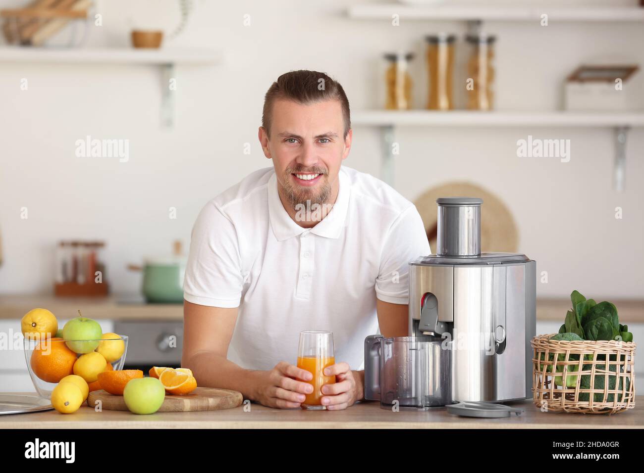Young man with glass of fresh fruit juice near modern juicer in kitchen ...