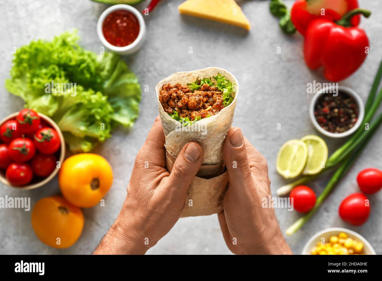 Man with tasty burrito and ingredients on grey background Stock Photo ...