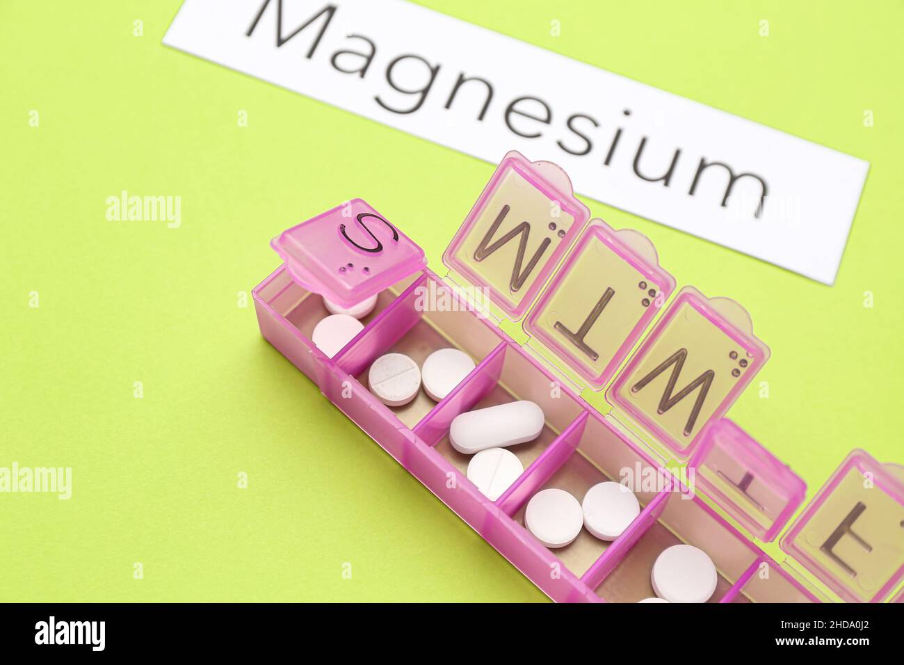 Plastic container with pills and word MAGNESIUM on green background ...