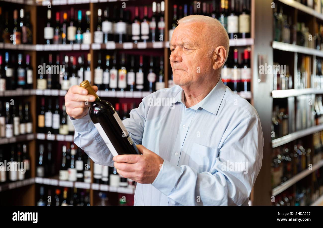 Elderly man chooses red wine in a liquor store Stock Photo - Alamy