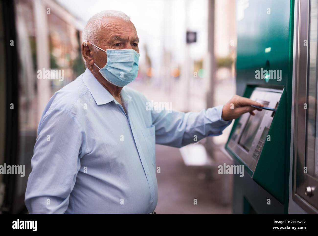 Old man in mask using cash machine on tram station Stock Photo - Alamy