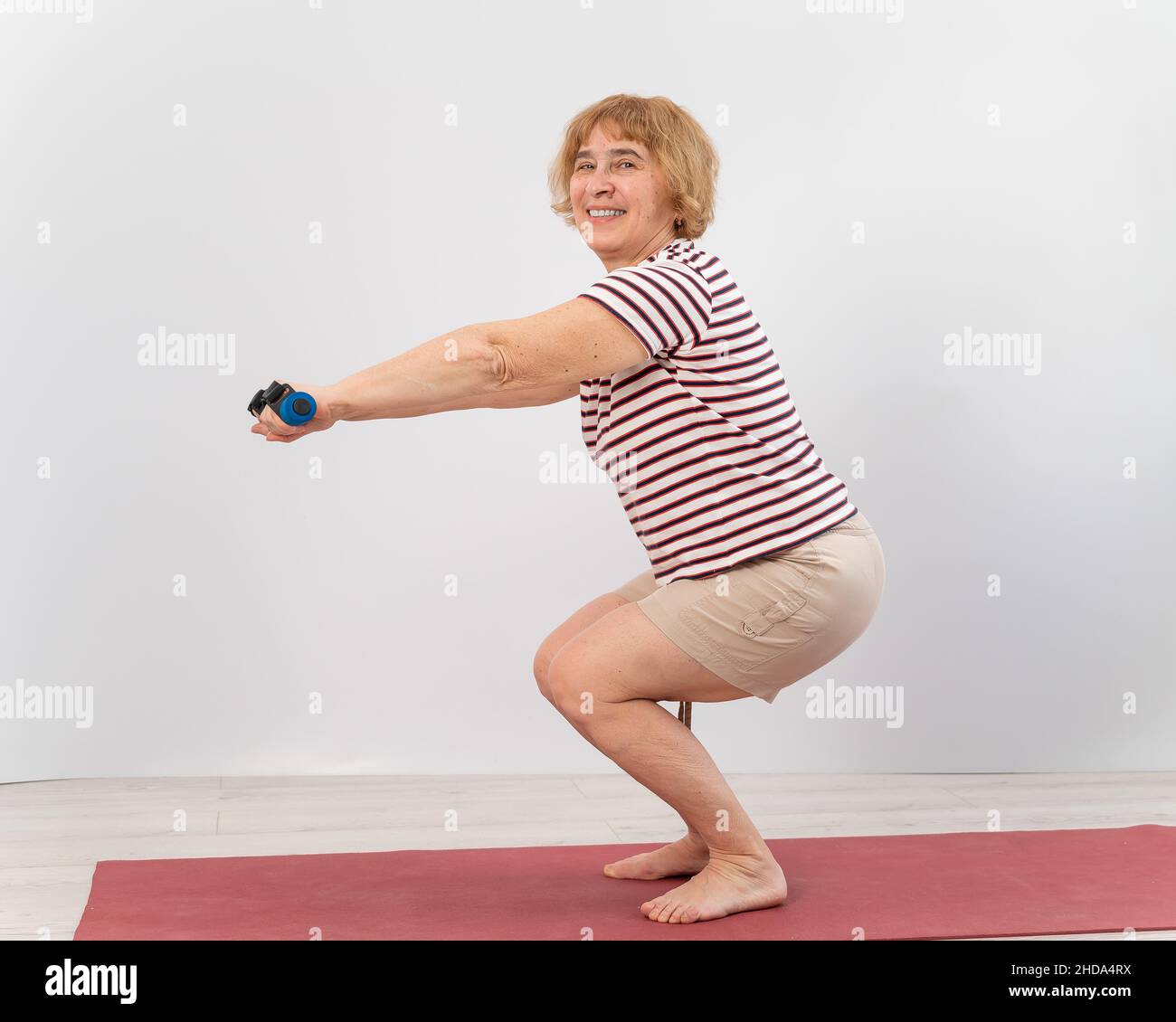 Elderly woman doing squats on a white background. The old lady is doing ...