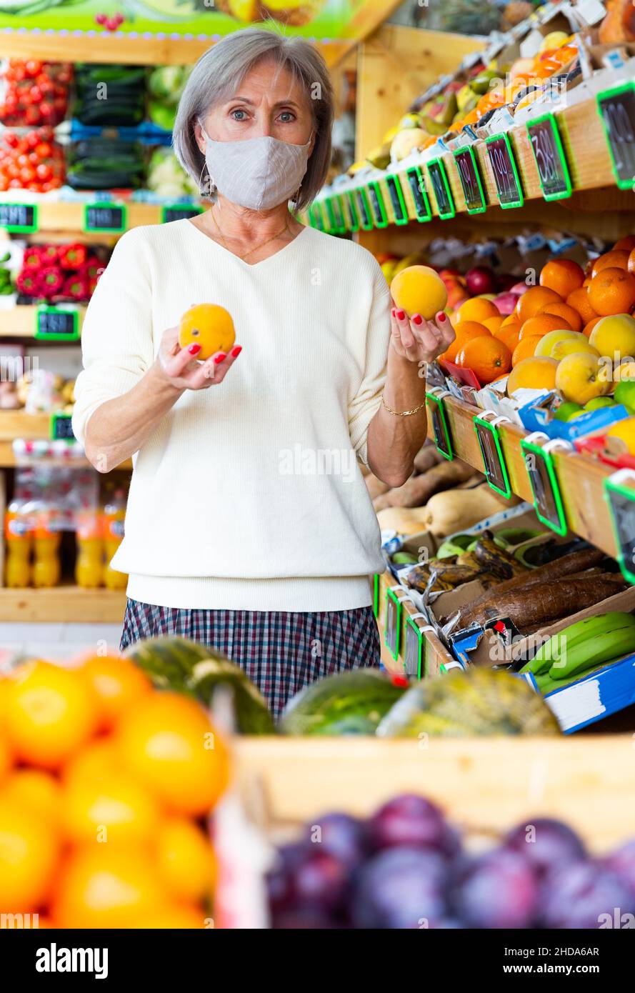 Woman in protective mask choosing sweet tangerines and other fruit on ...