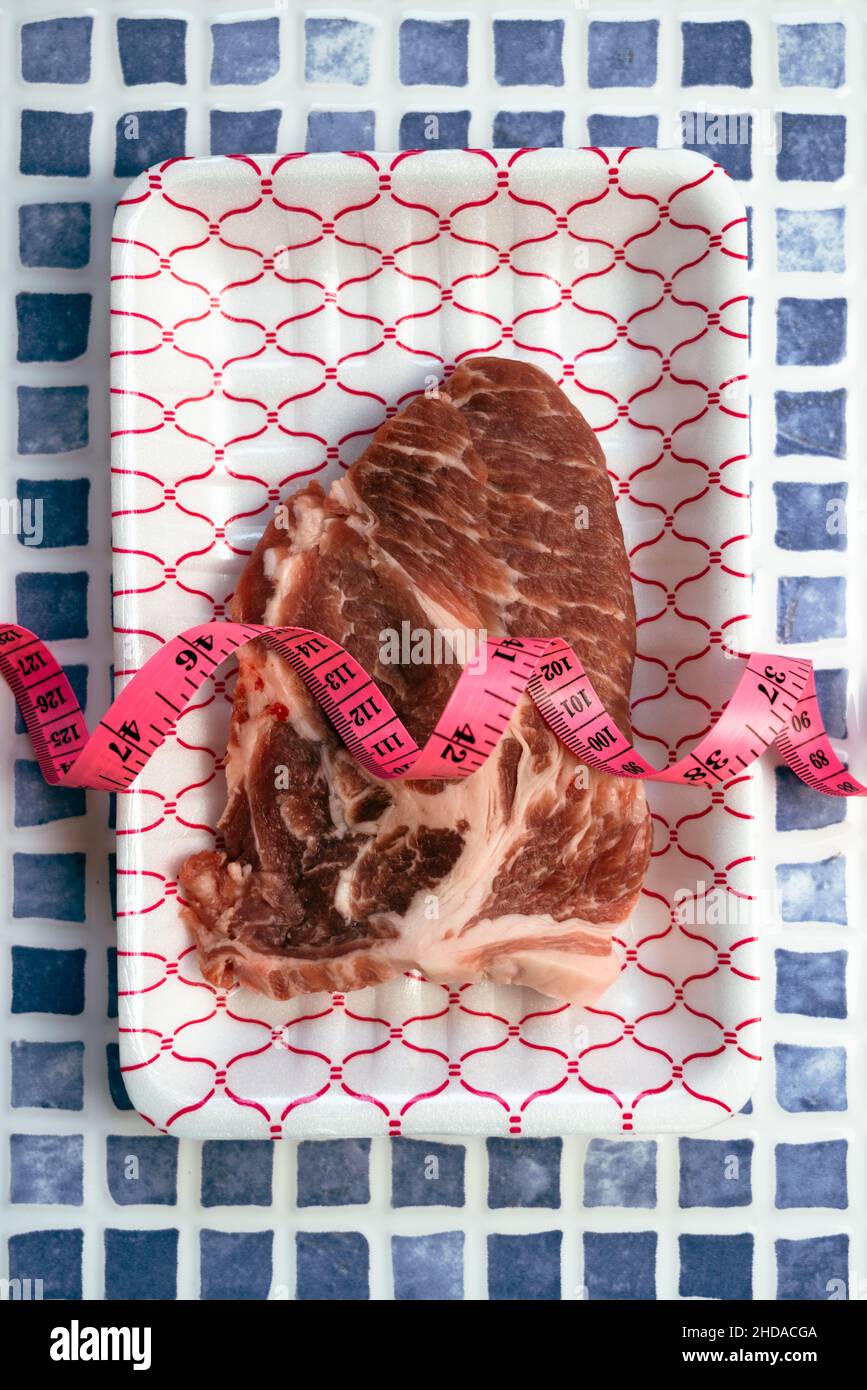 Fresh pork neck meat and tape measure in packaging tray on blue tile ...