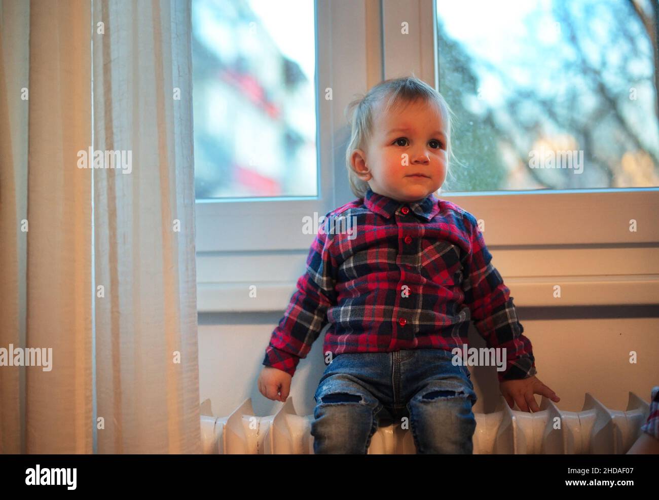 Cute little boy sitting on a radiator against the window Stock Photo ...