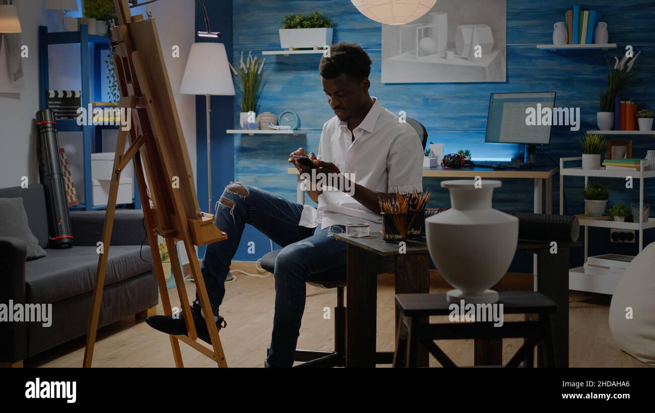 Black young artist with smartphone seeking inspiration for masterpiece ...