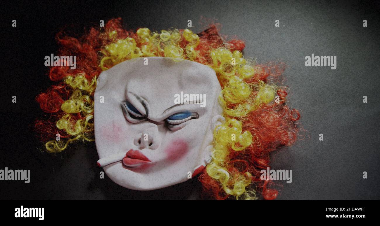 Scary clown mask falling over grey surface against flickering ...