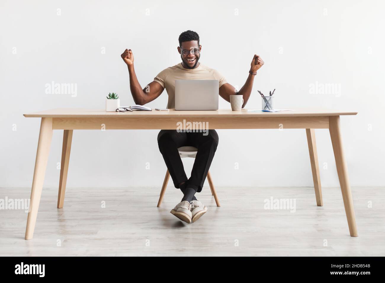 Successful black man making YES gesture while working on laptop at desk ...