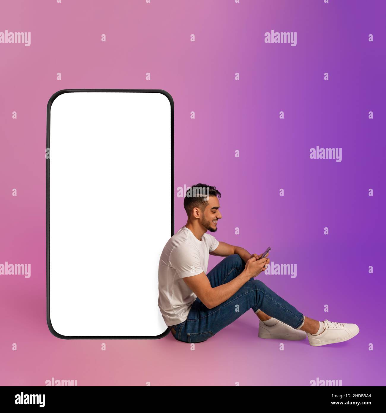 Cheery Arab guy sitting near big cellphone with blank screen, using ...