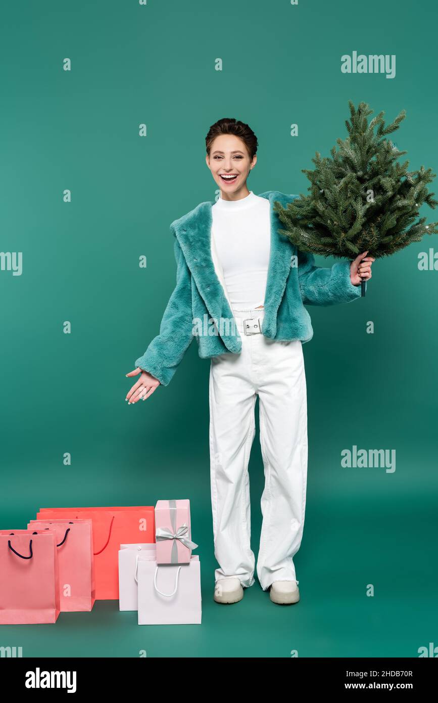 full length view of happy and trendy woman with small christmas tree ...