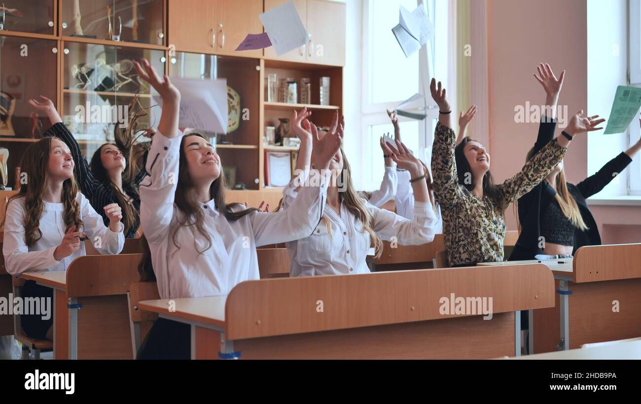 Pupils sitting at their desks in the classroom throw notebooks up ...