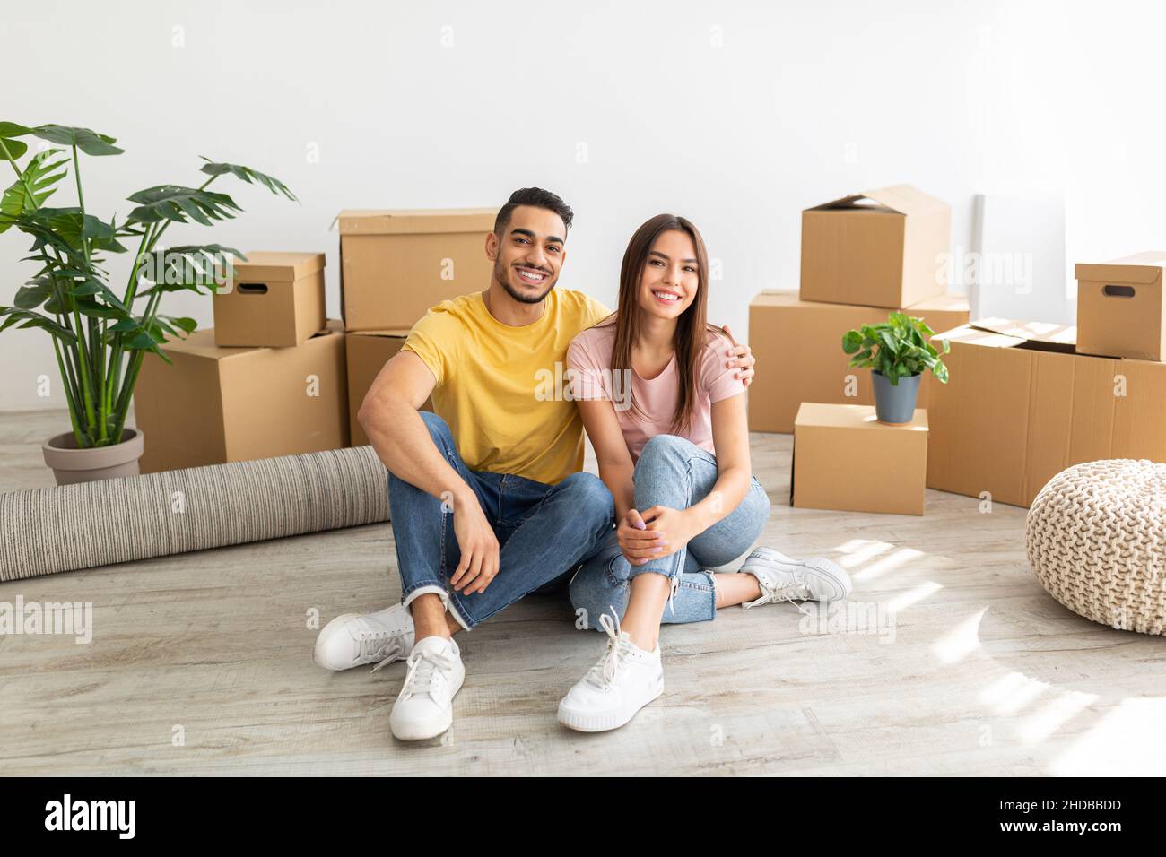 Full length portrait of loving multinational couple sitting on floor ...