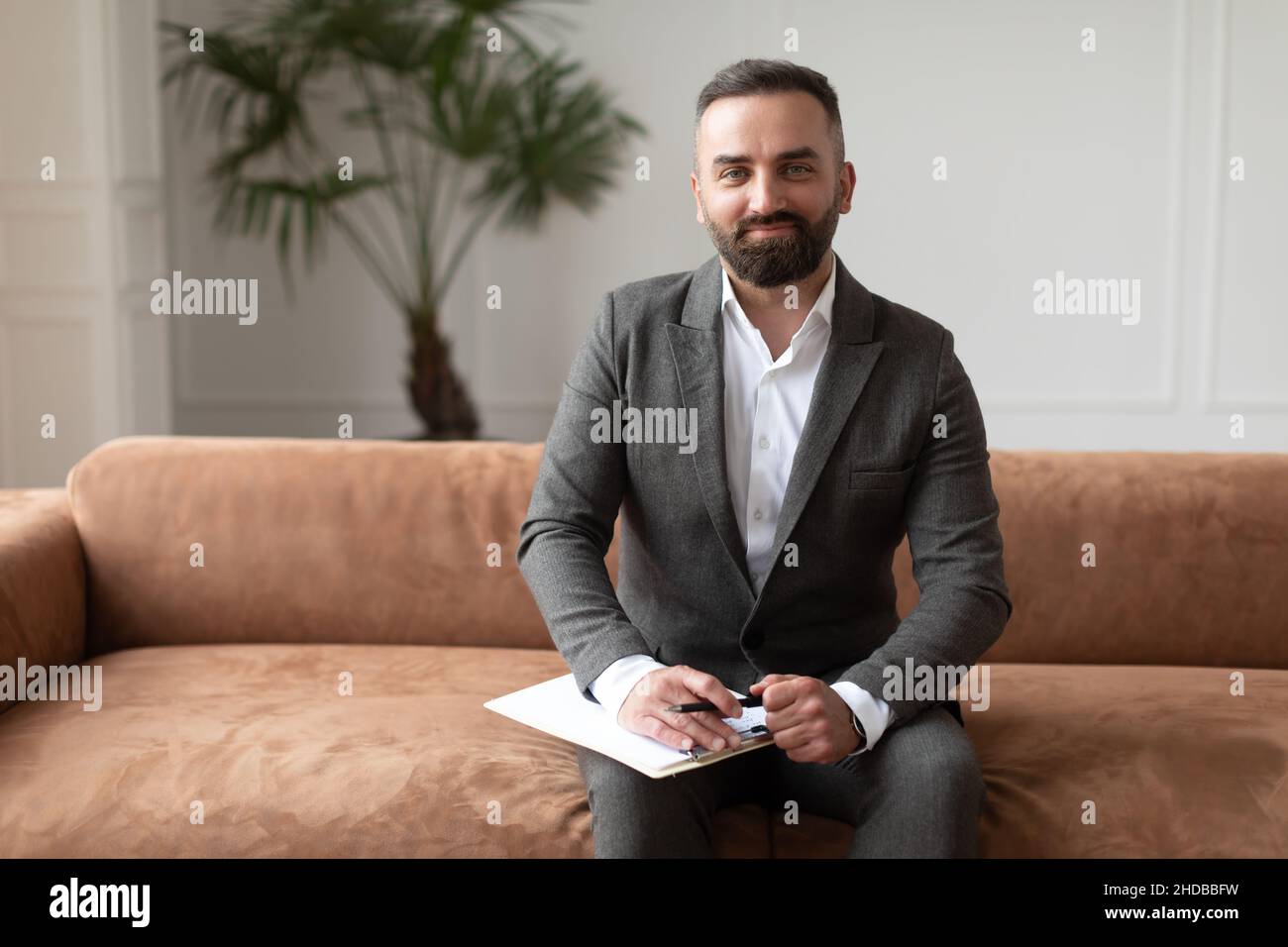 Portrait of confident male therapist in suit sitting on sofa Stock ...