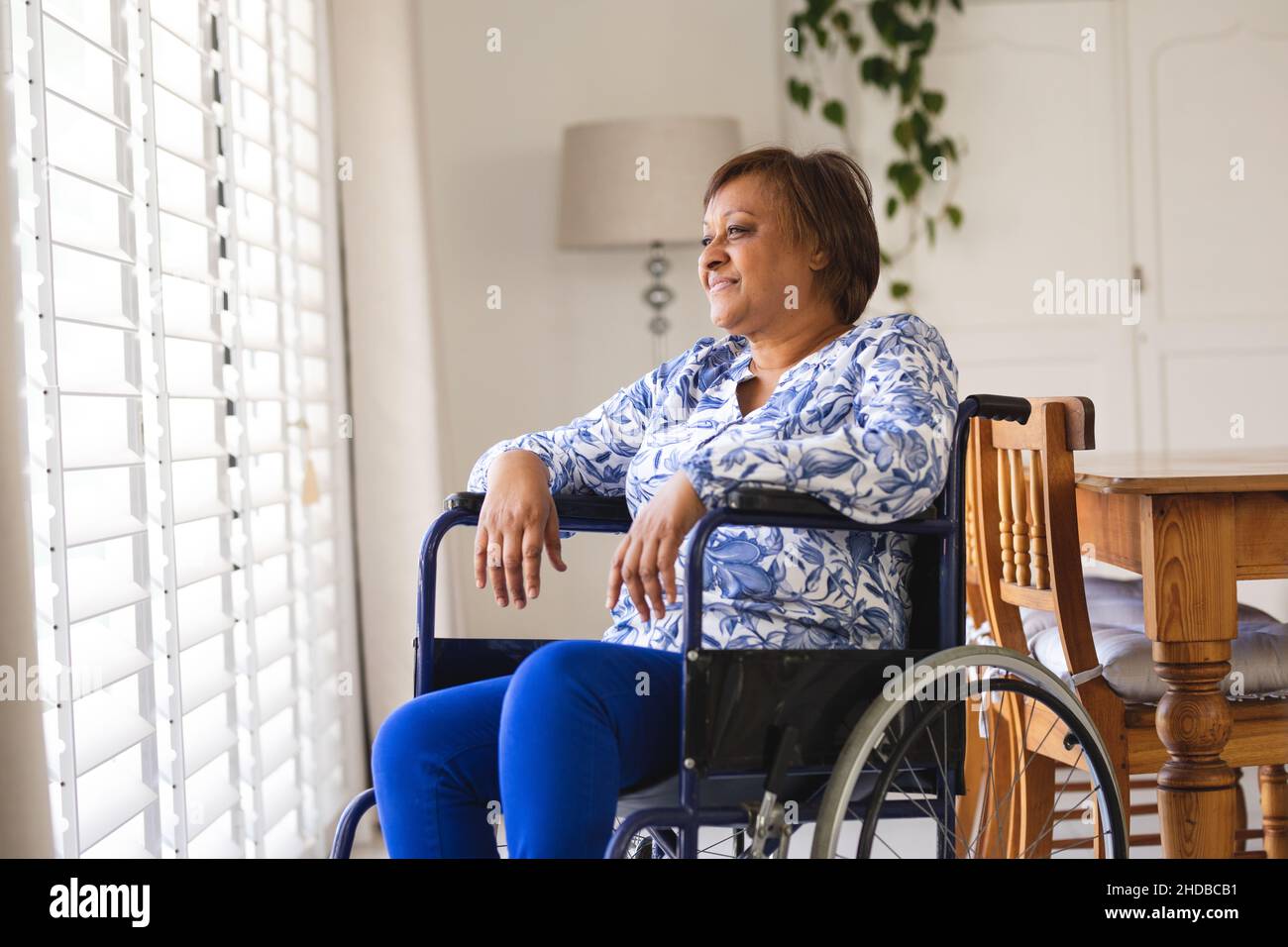 Smiling disabled senior woman looking through window shutter while ...
