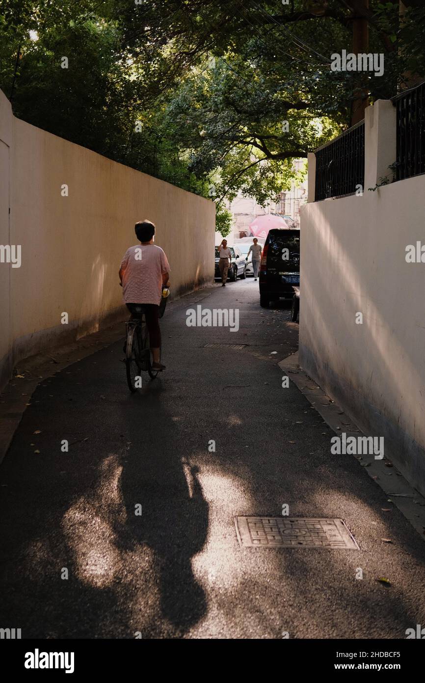 Vertical back view of a person biking through an alley Stock Photo - Alamy