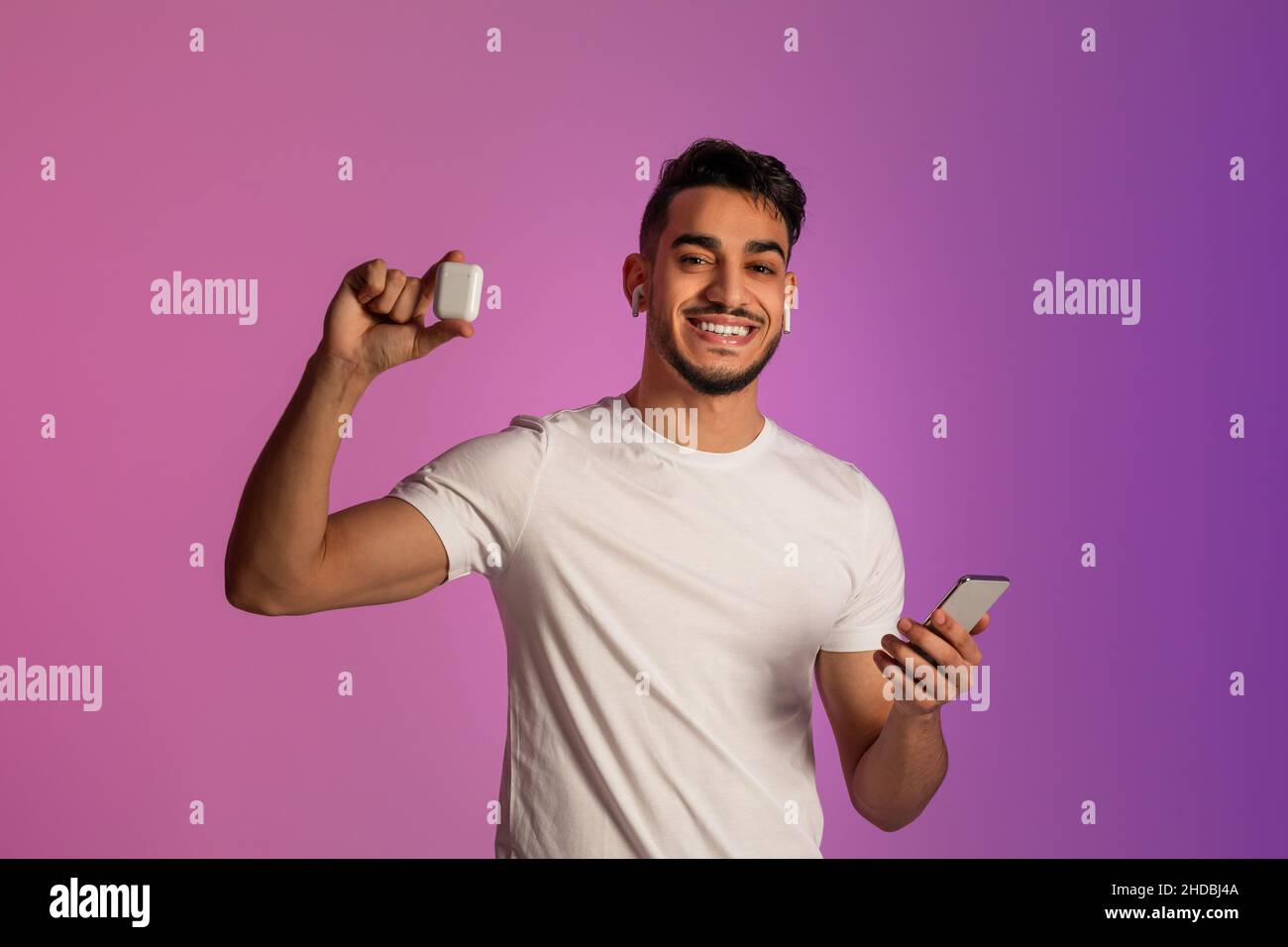 Smiling Arab guy with smartphone advertising wireless earphopnes ...
