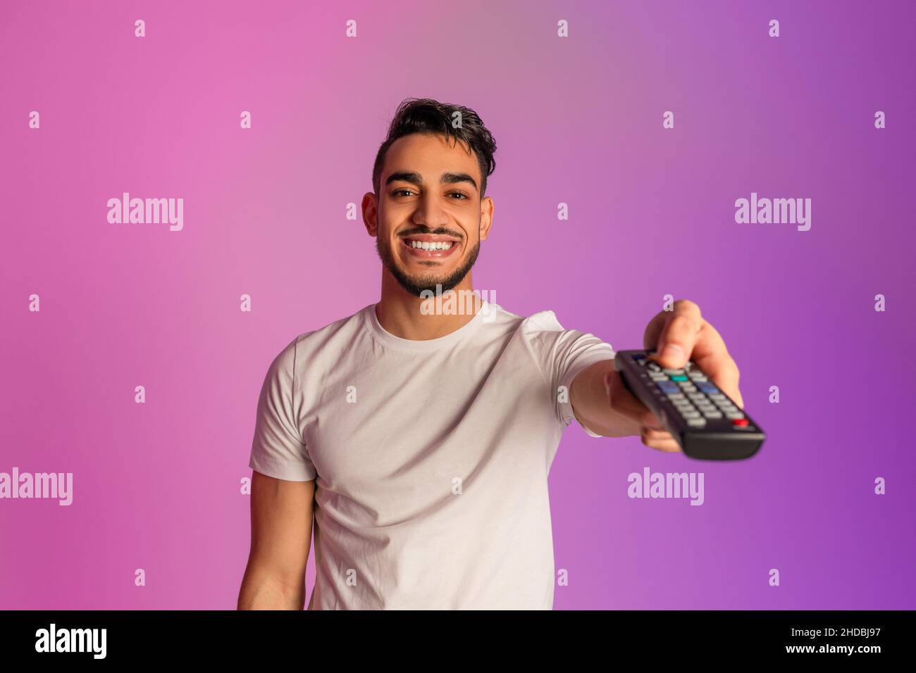 Positive young Arab guy watching TV, switching channels with remote ...