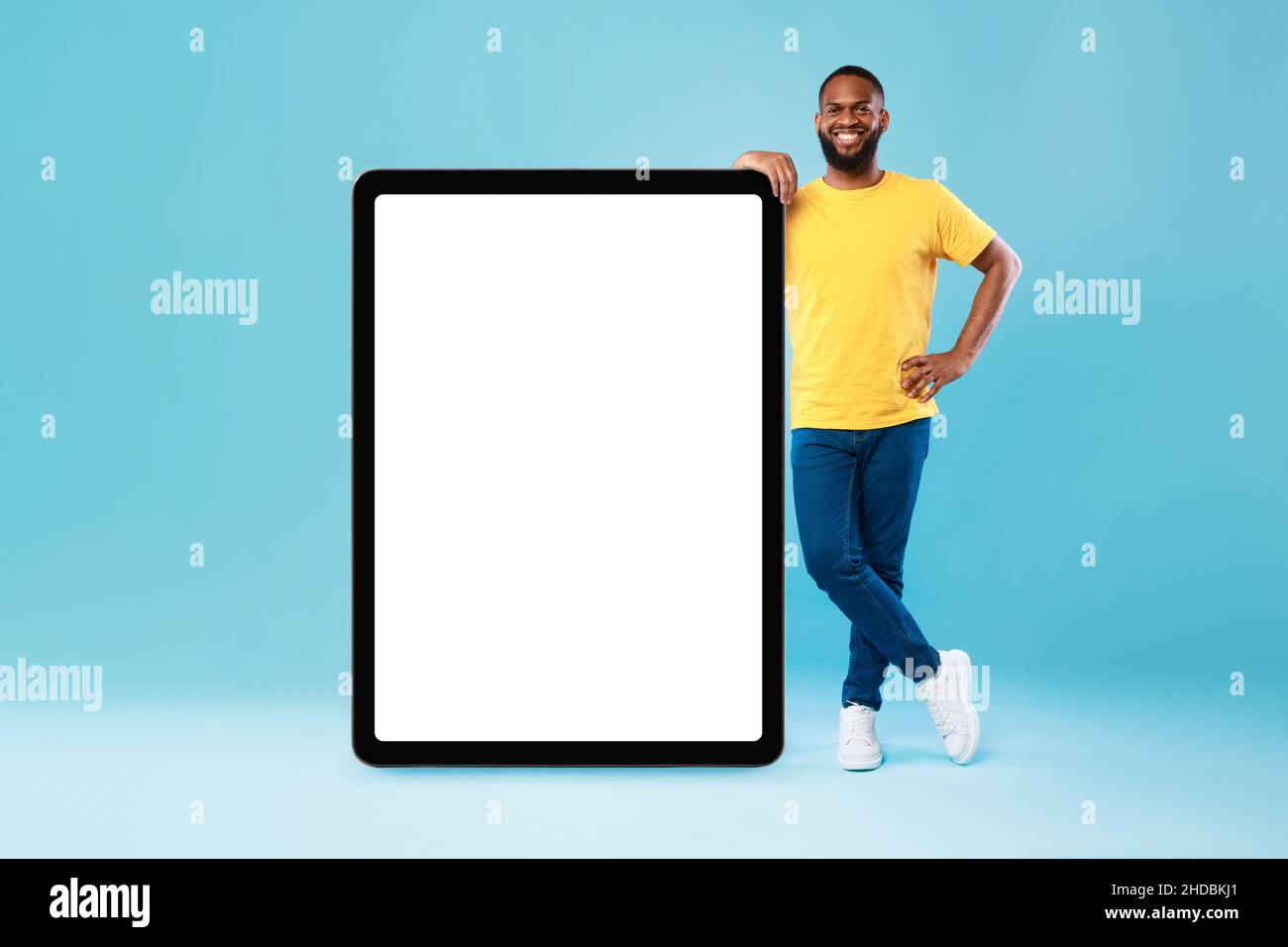 Cheerful young black guy leaning on giant tablet pc, demonstrating ...