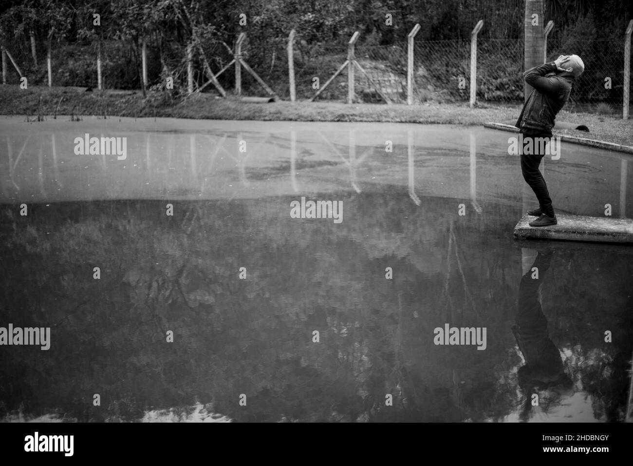 A grayscale of a desperate person standing on a small pier at the ...