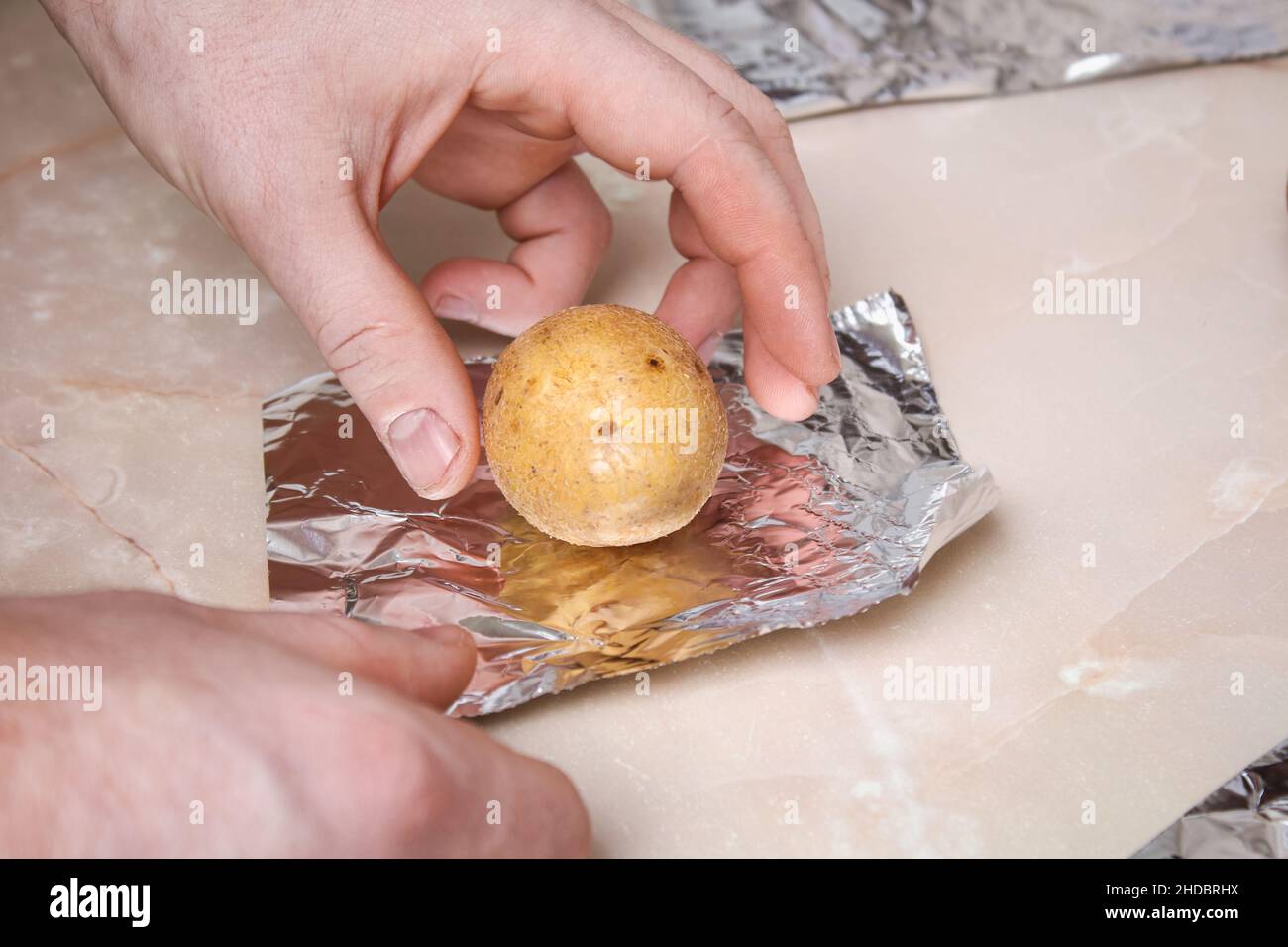 The man wraps peeled raw potatoes in foil and places them on the wire ...