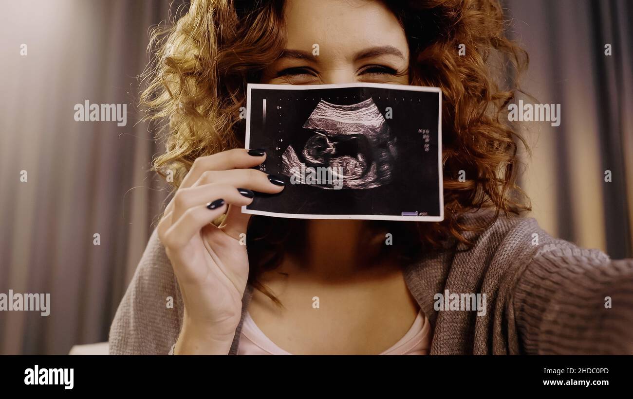 Curly woman covering face with ultrasound scan of baby at home Stock ...