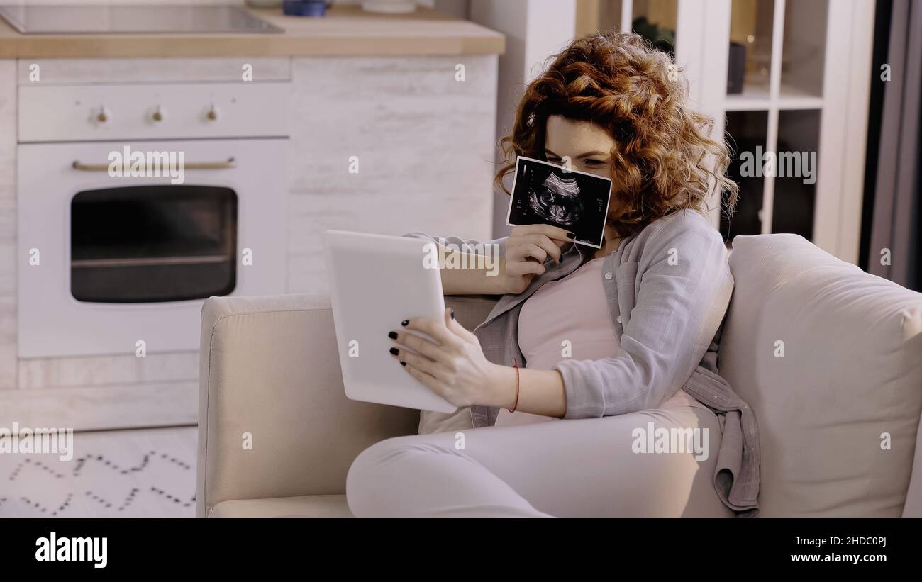 Pregnant woman holding ultrasound scan of baby during video call on ...