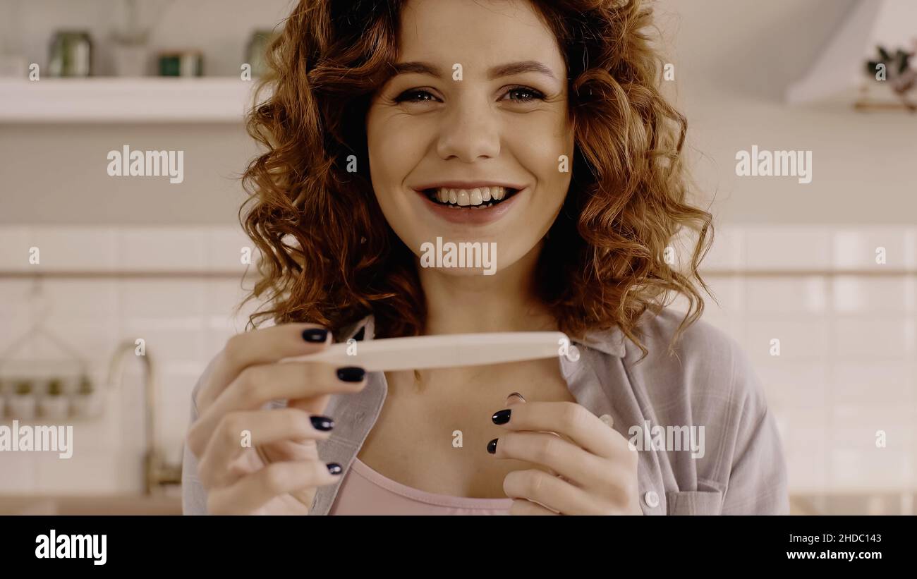Positive woman holding blurred pregnancy test and looking at camera at ...