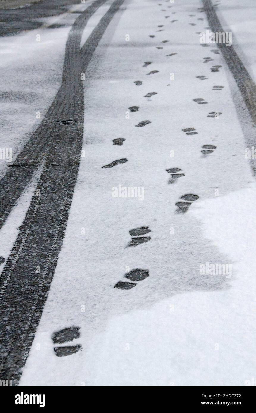 Traces of car tyres and footprints on thin snow cover of asphalt road ...