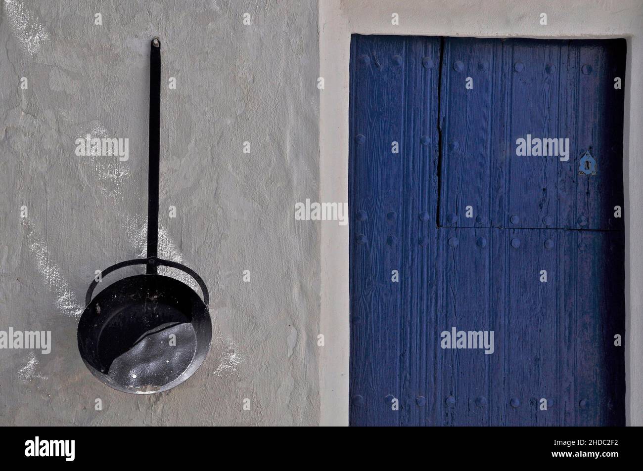 Long-handled pan on house wall with blue front door, Spain, Europe ...