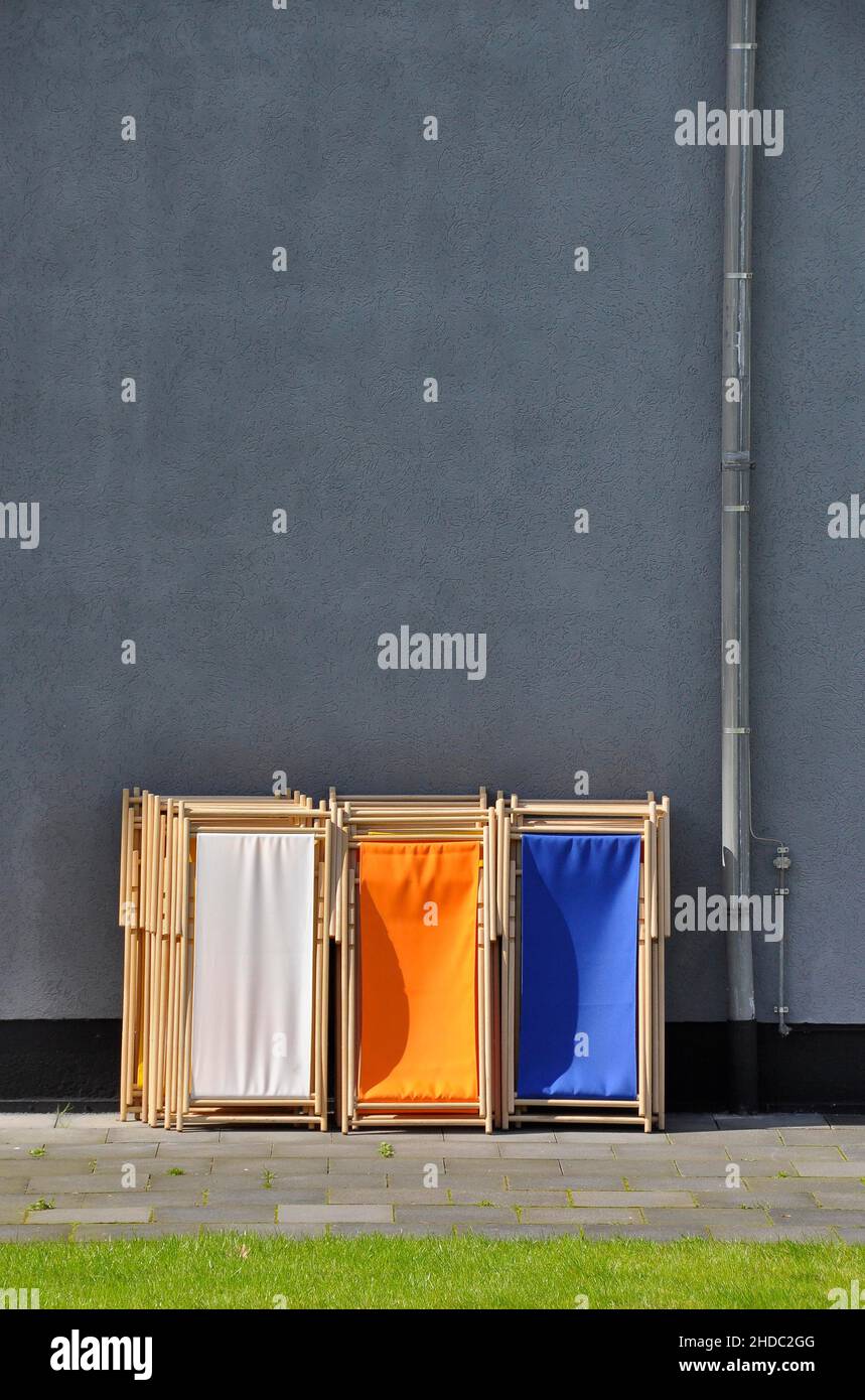 Grey wall with gutter, coloured deck chairs in park, Cologne, Germany ...