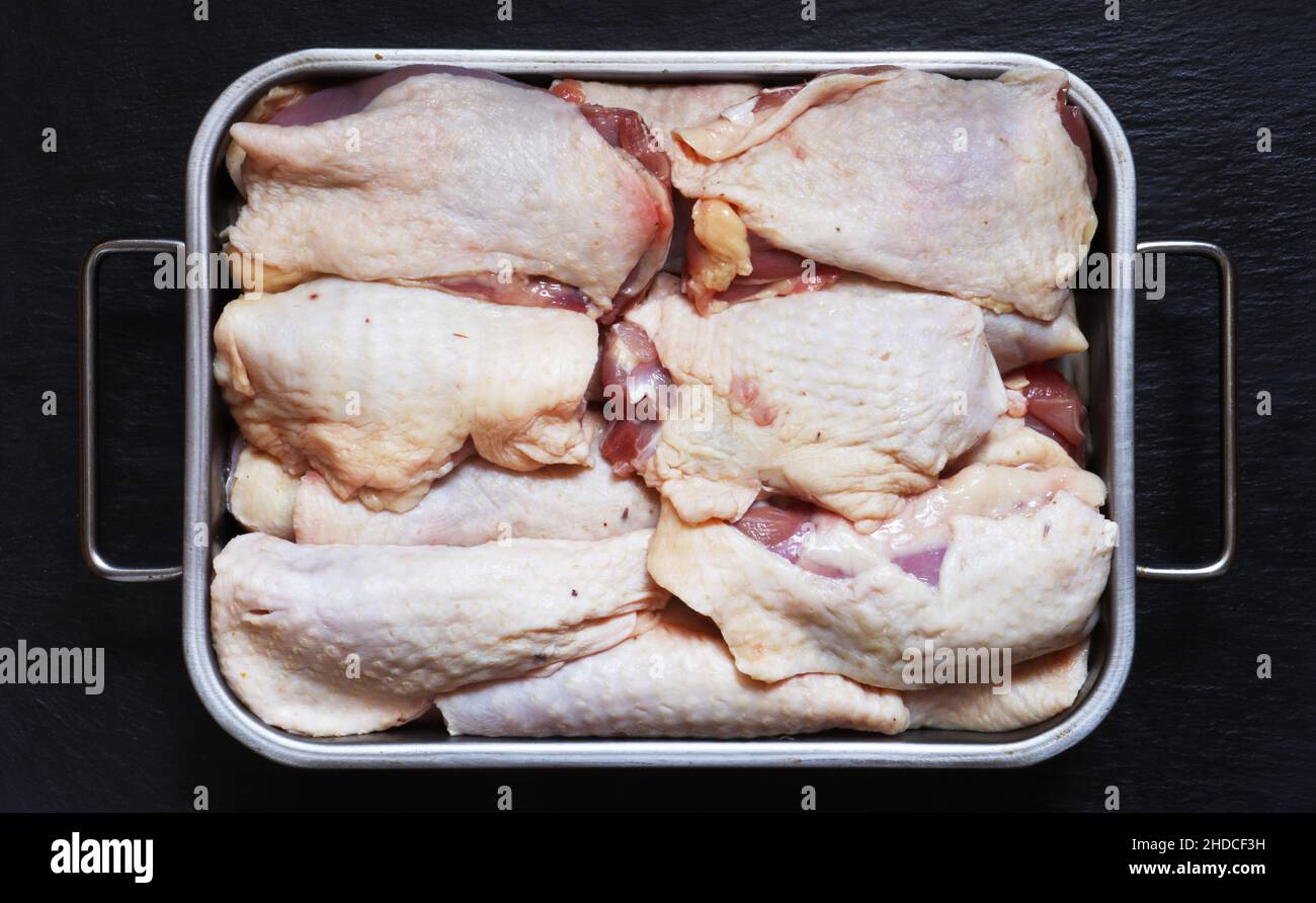 Photography of raw, boneless chicken thighs in a metal bin on slate ...