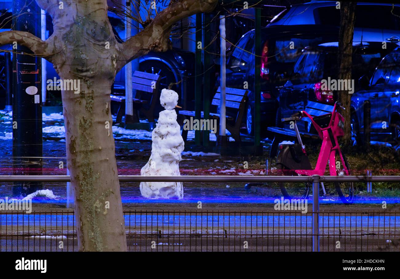 a sad snowman alone on the streets at night. Snow has almost melted ...