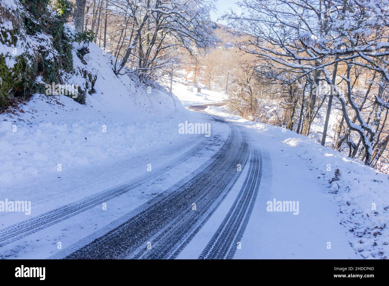 An empty road with a tricky left turn covered with snow. Tyre traces ...
