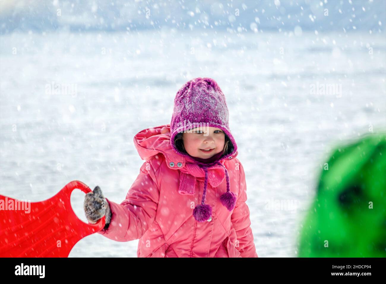A girl in pink clothes rides on a snowy slide in winter. White girl 5 ...